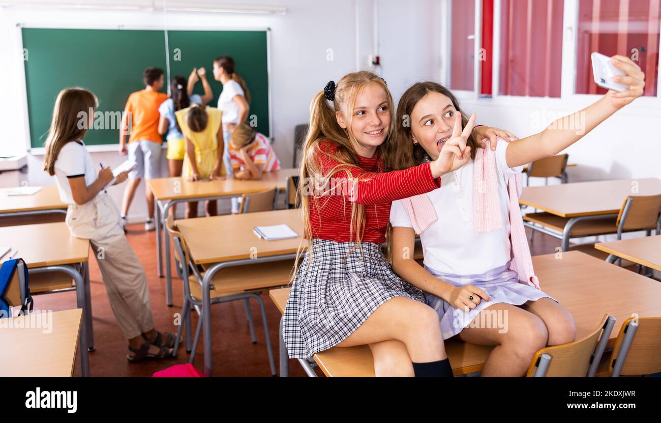 Two cheerful schoolgirls take a selfie during recess in classroom Stock ...