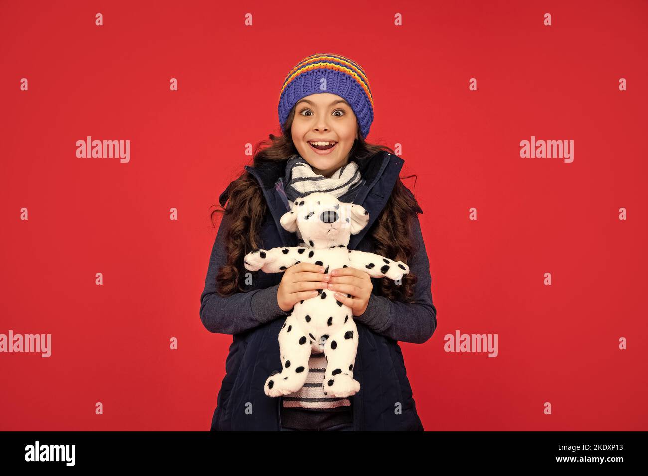 surprised child in puffer jacket hold toy. teen girl on red background ...