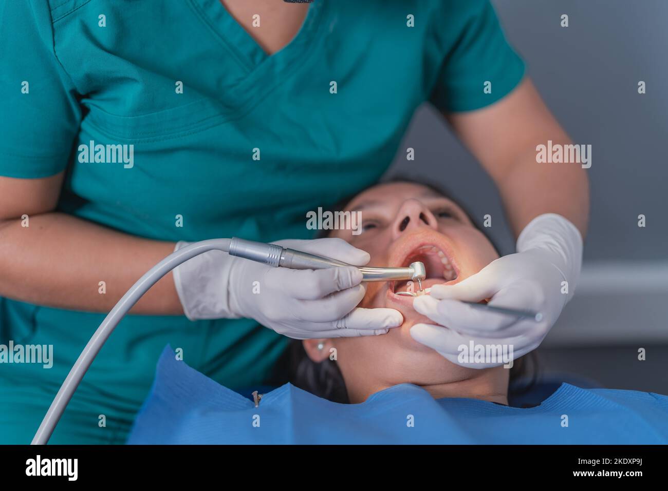 Crop unrecognizable dentist in green uniform drilling teeth of ethnic ...