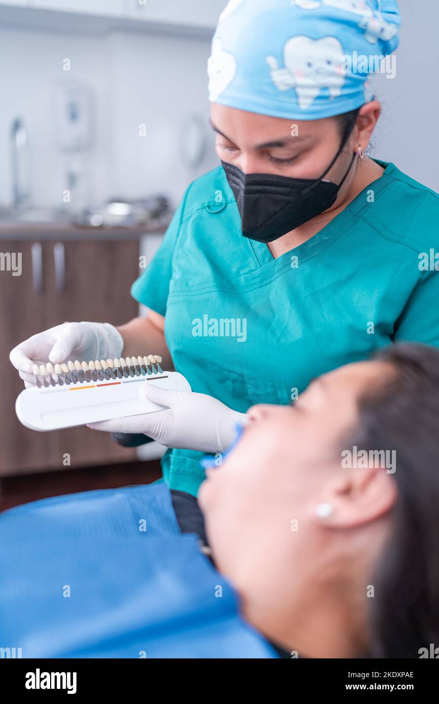 Concentrated young ethnic female dentist in uniform and mask choosing ...