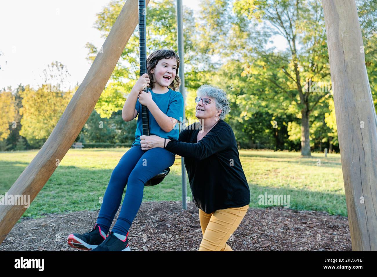 Grandma in casual clothes with glasses pushing swing with laughing ...