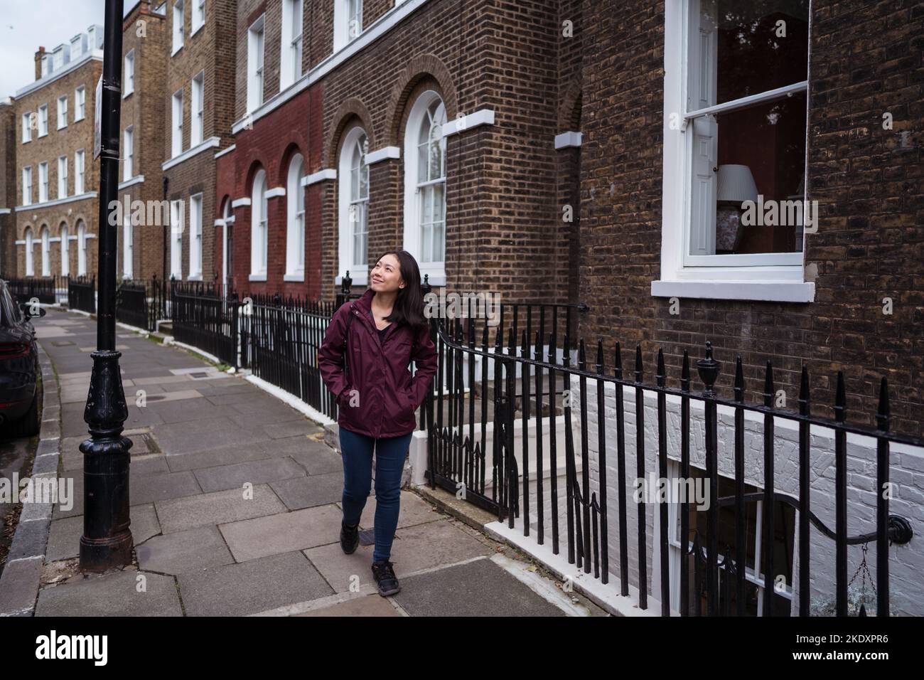 Positive Asian female in outerwear holding hands in pockets and looking ...