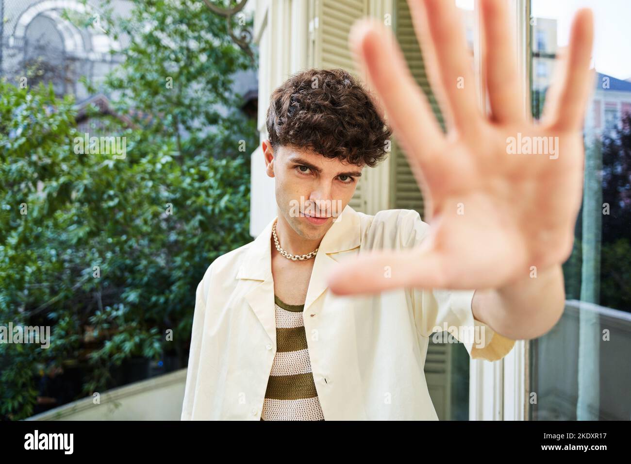 Young male with curly hair in white shirt standing against glass walls ...