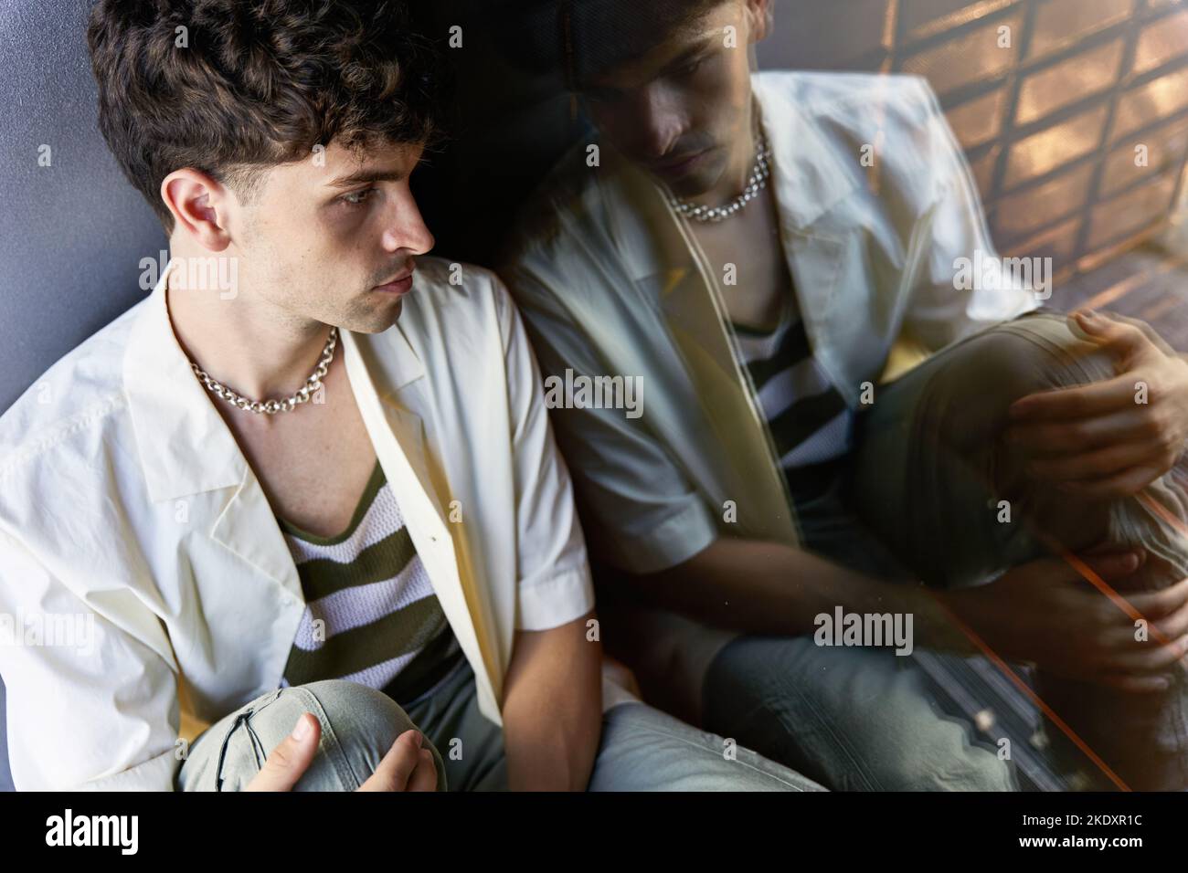From above unhappy young male in casual clothes embracing knee and ...