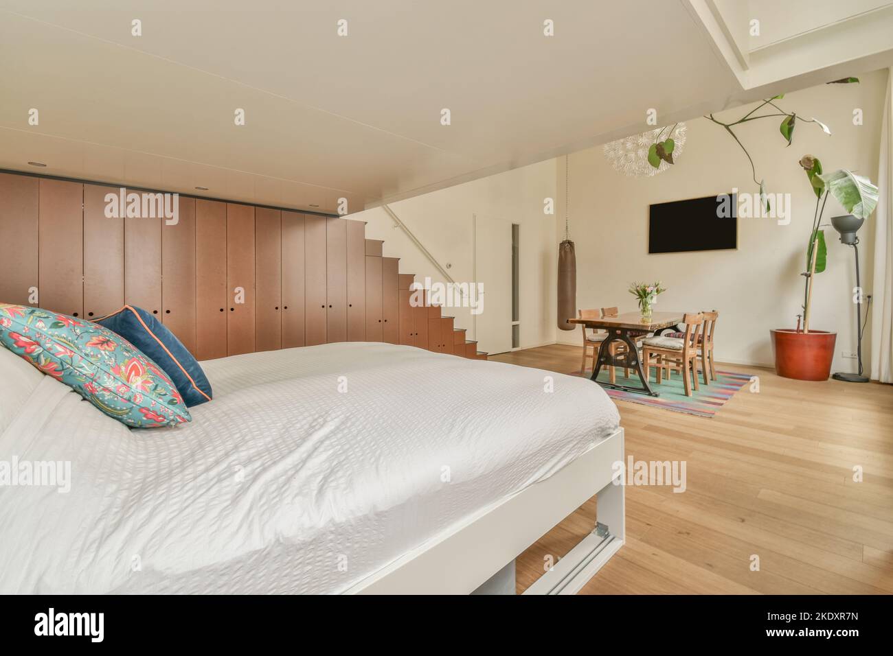 Comfortable bed with blanket and pillows placed in front of television ...