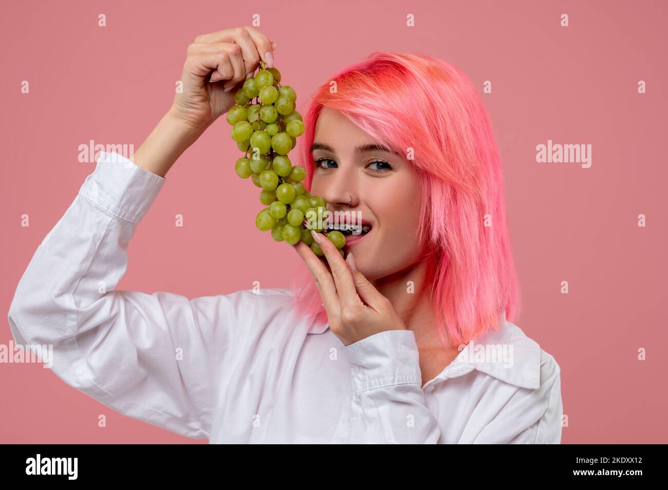 Beautiful pink-haired young female eating delicious fruit Stock Photo ...