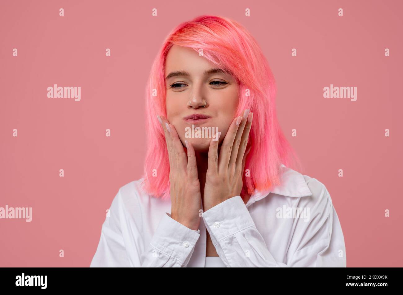 Pleased pink-haired girl touching her face while chewing Stock Photo ...