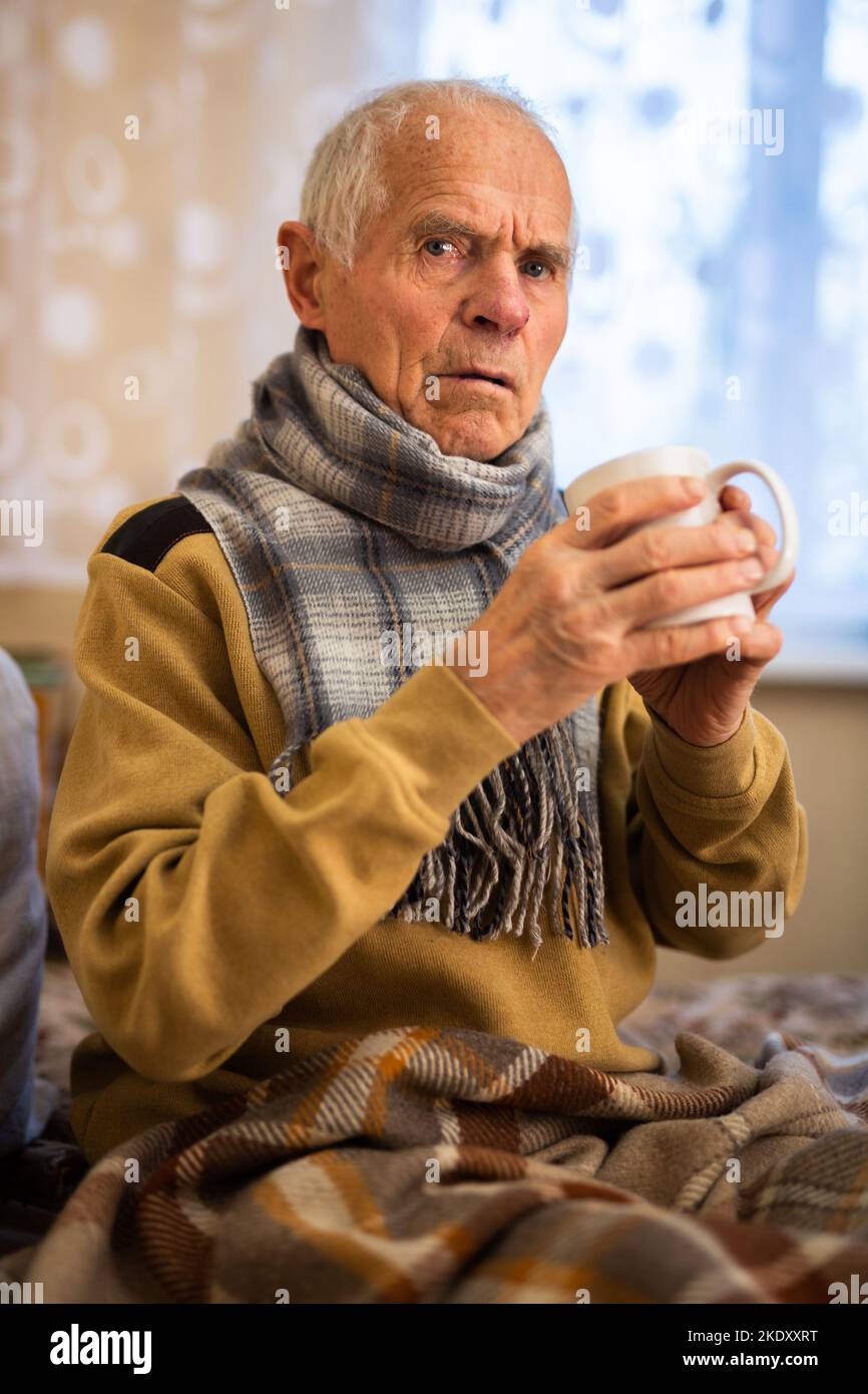 old man wrapped in blanket has cold and drinks hot infusion Stock Photo ...