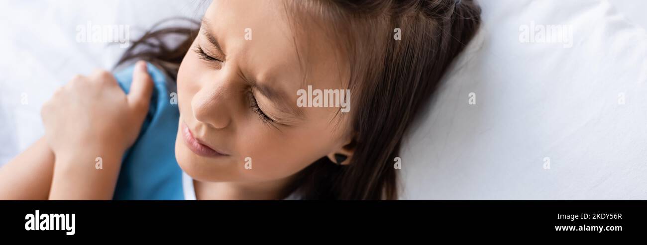 High angle view of ill child touching shoulder while lying on bed in ...