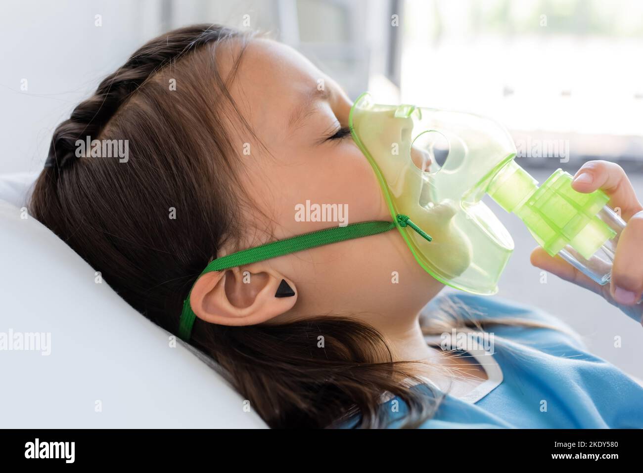 Diseased kid holding oxygen mask while lying on bed in clinic,stock ...
