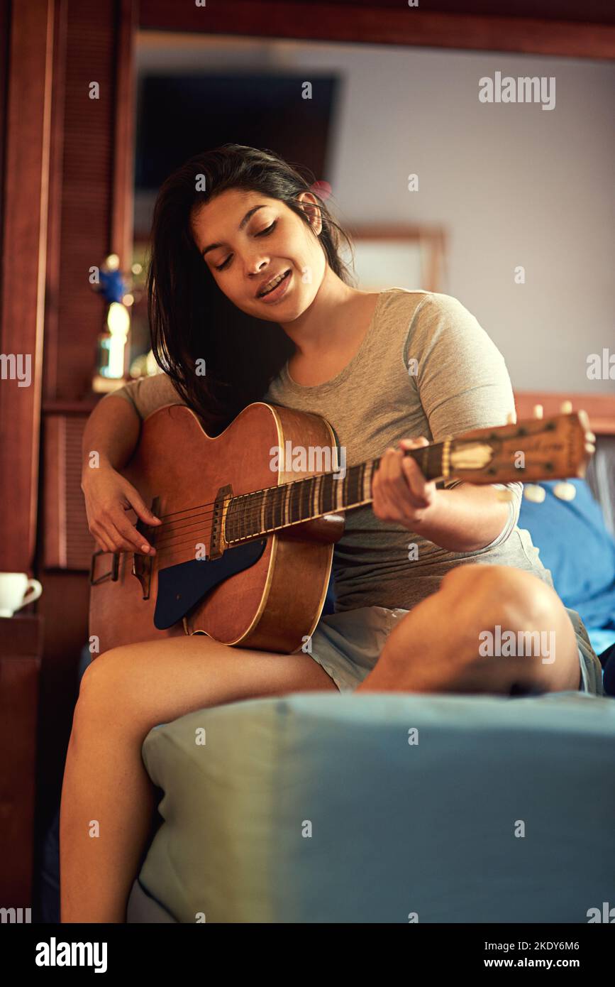 Solo serenades. a happy young woman playing her guitar while sitting on her bed Stock Photo - Alamy