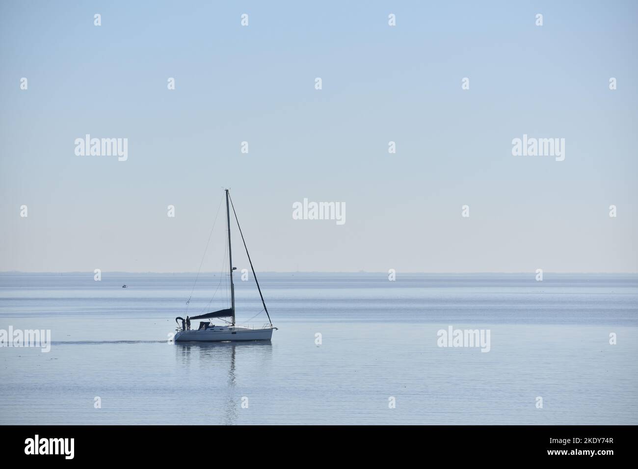 A single sailboat sailing on clear blue waters under a bright sky Stock ...