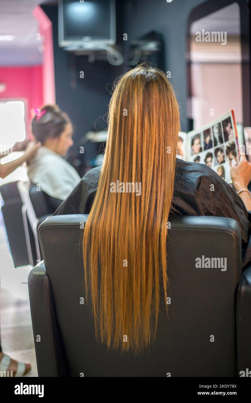 Rear view of woman sitting on hairdresser chair choosing a hairstyle ...