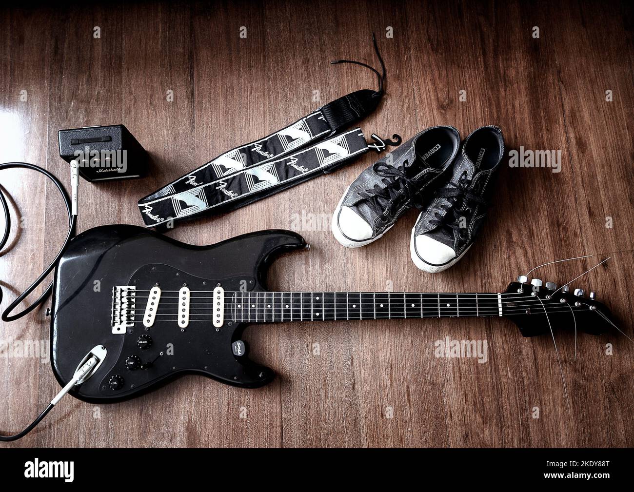 A flat lay of a black electric guitar plugged into a small amp with a ...