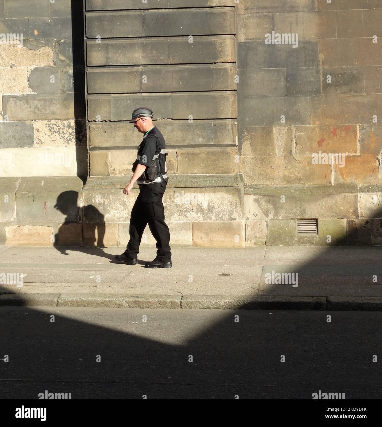 A male in a cap walking on a sidewalk in Glasgow on a sunny day Stock ...
