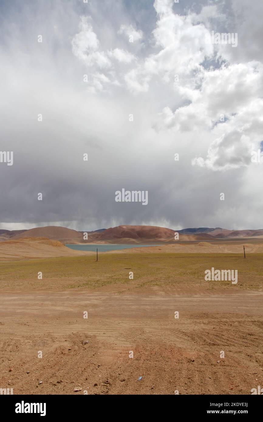 A landscape with a lake and rocky dirt ground with mountains against ...