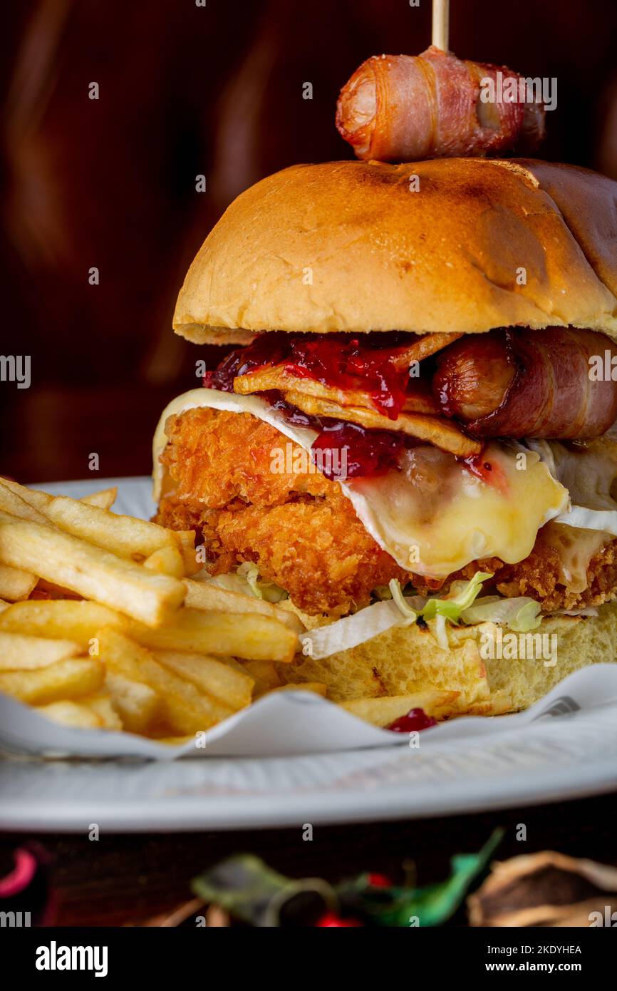 A vertical closeup of a burger with fried nuggets, sausages wrapped in ...