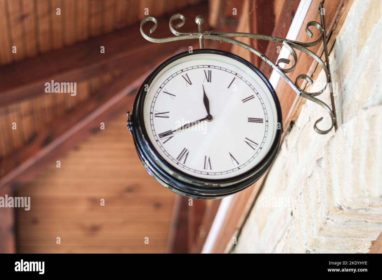 A round clock with black sides and roman numerals attached to the wall ...