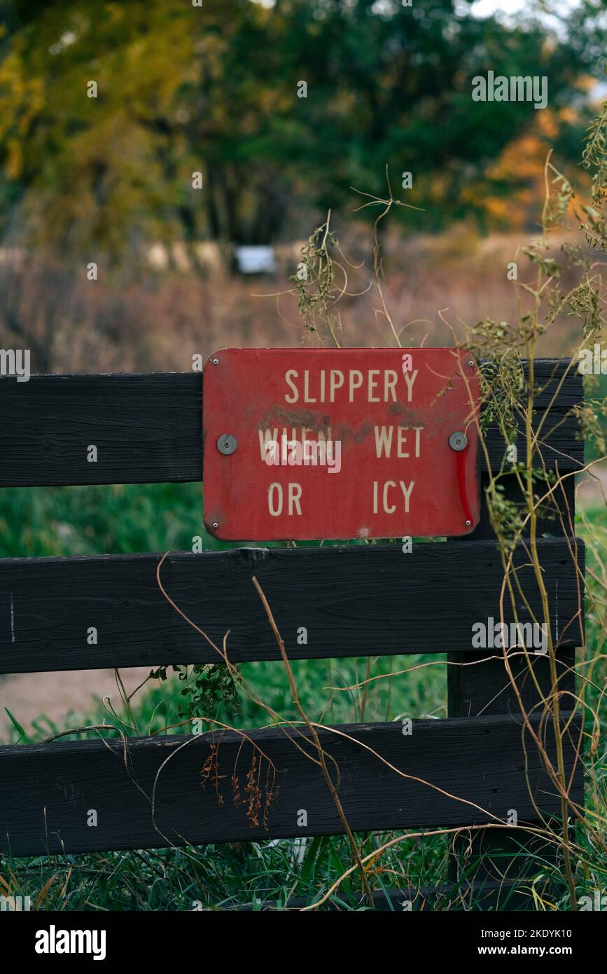 The vertical view of a slippery floor warning sign on a wooden fence in ...