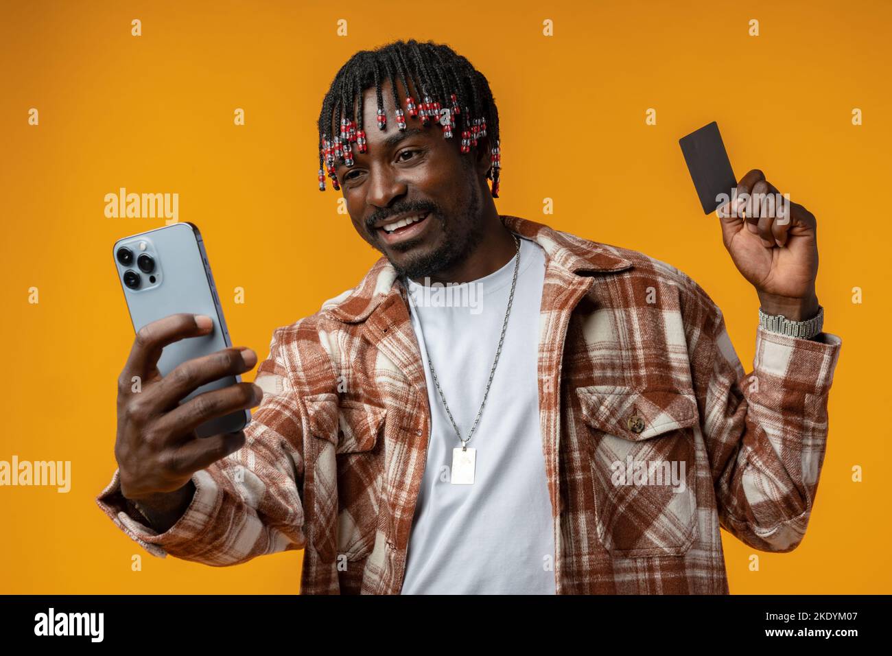 Smiling young african man on yellow background using mobile phone and ...