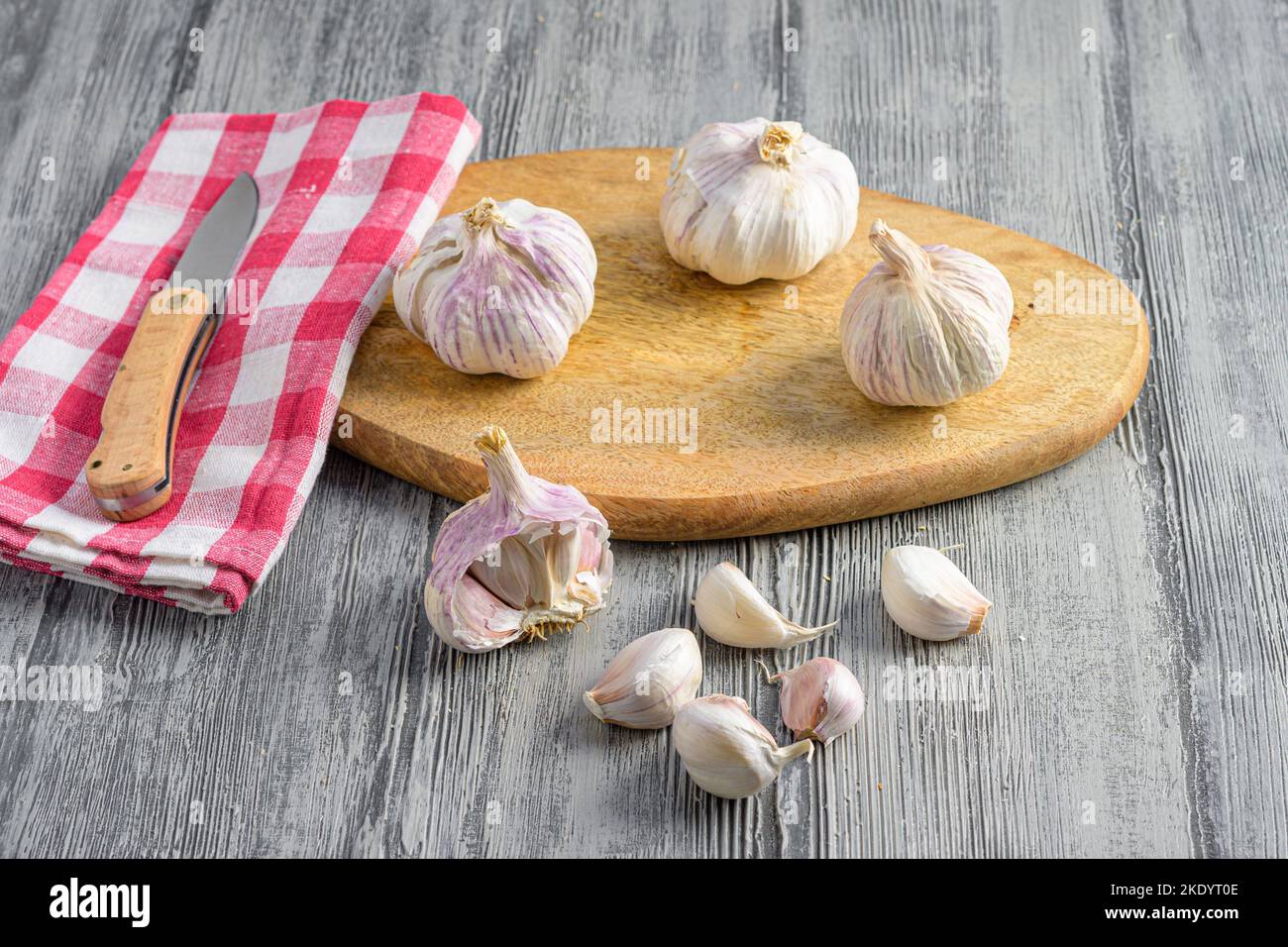 Several garlic on a wooden board next to a knife on a kitchen towel ...