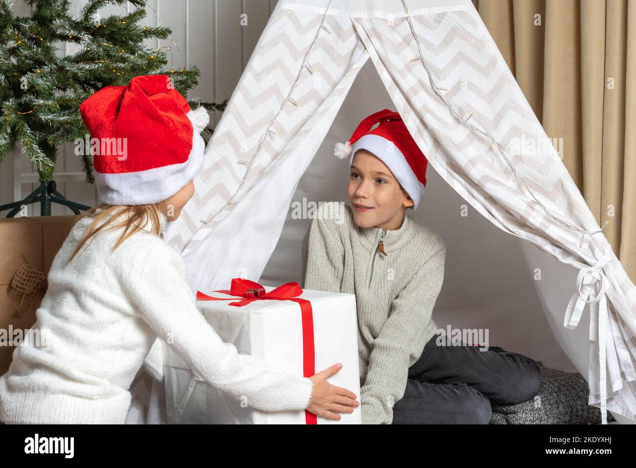 A girl in a Santa hat gives a gift to a boy for Christmas and New Year ...