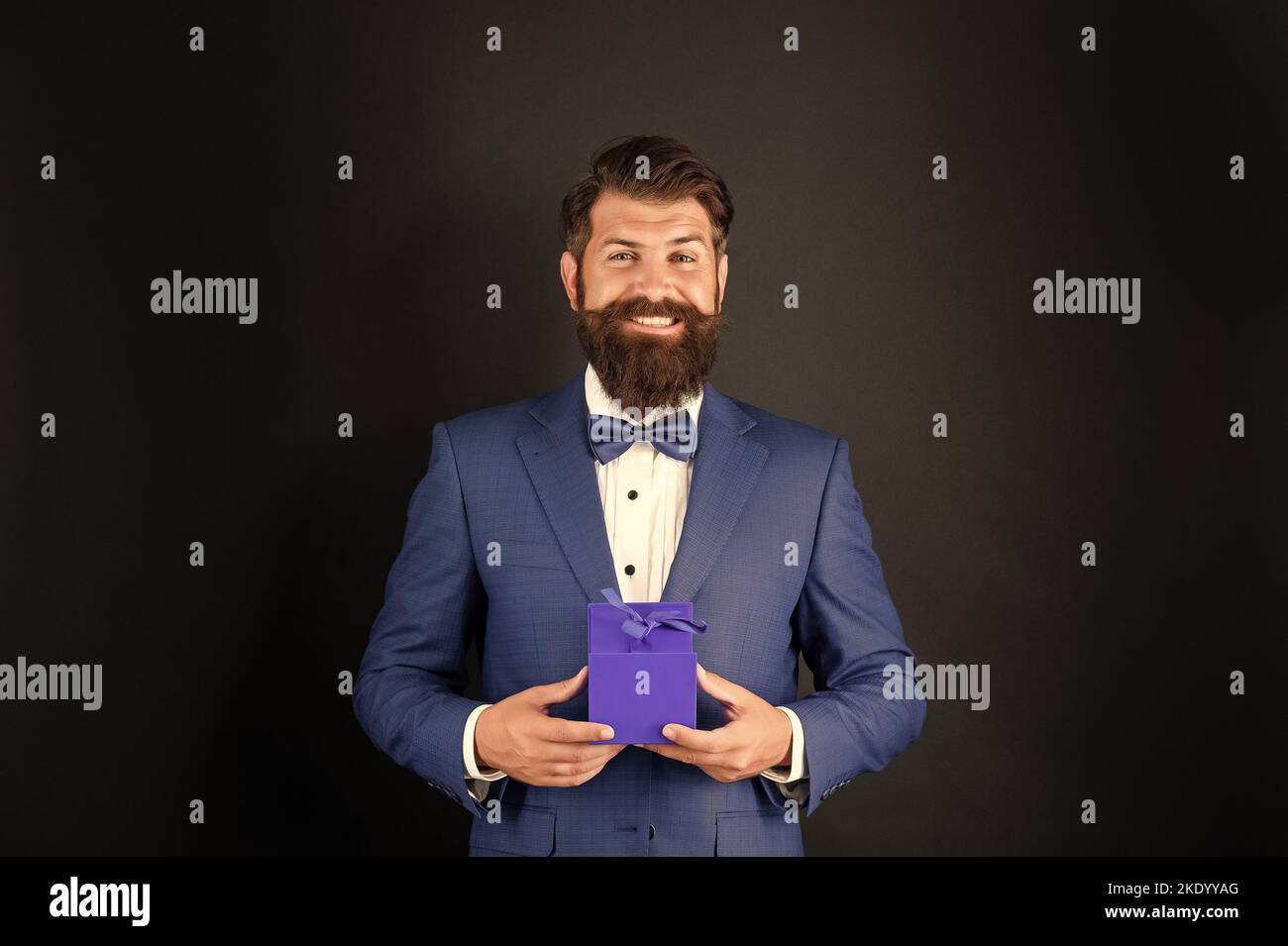 glad man in tuxedo bow tie formalwear on black background with gift box ...