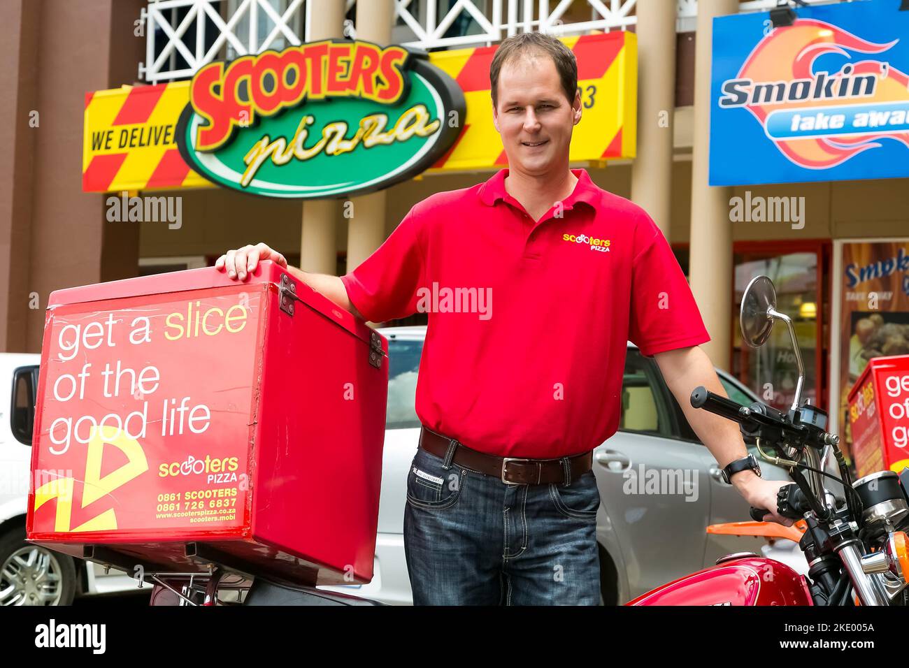 A food delivery man in a red uniform on the background of scooters ...