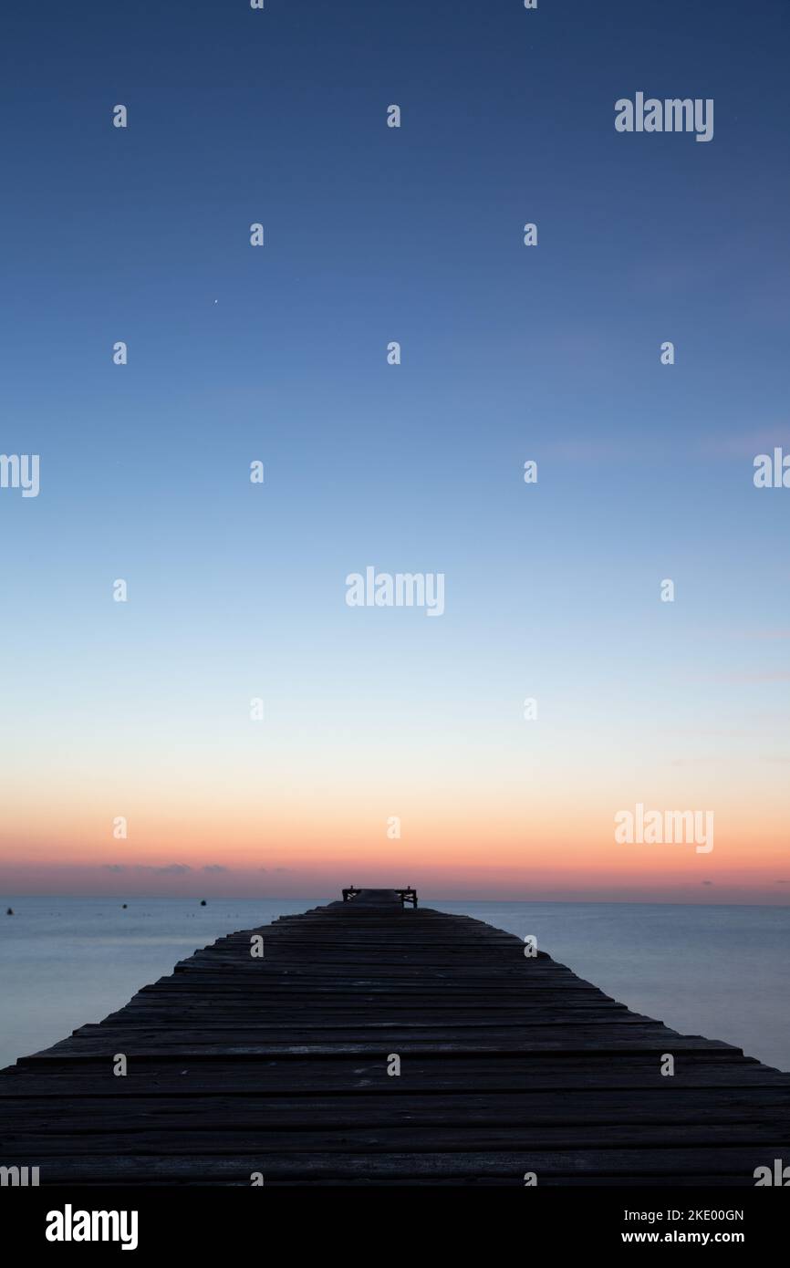 A vertical shot of a long pier in the sea at sunset Stock Photo - Alamy