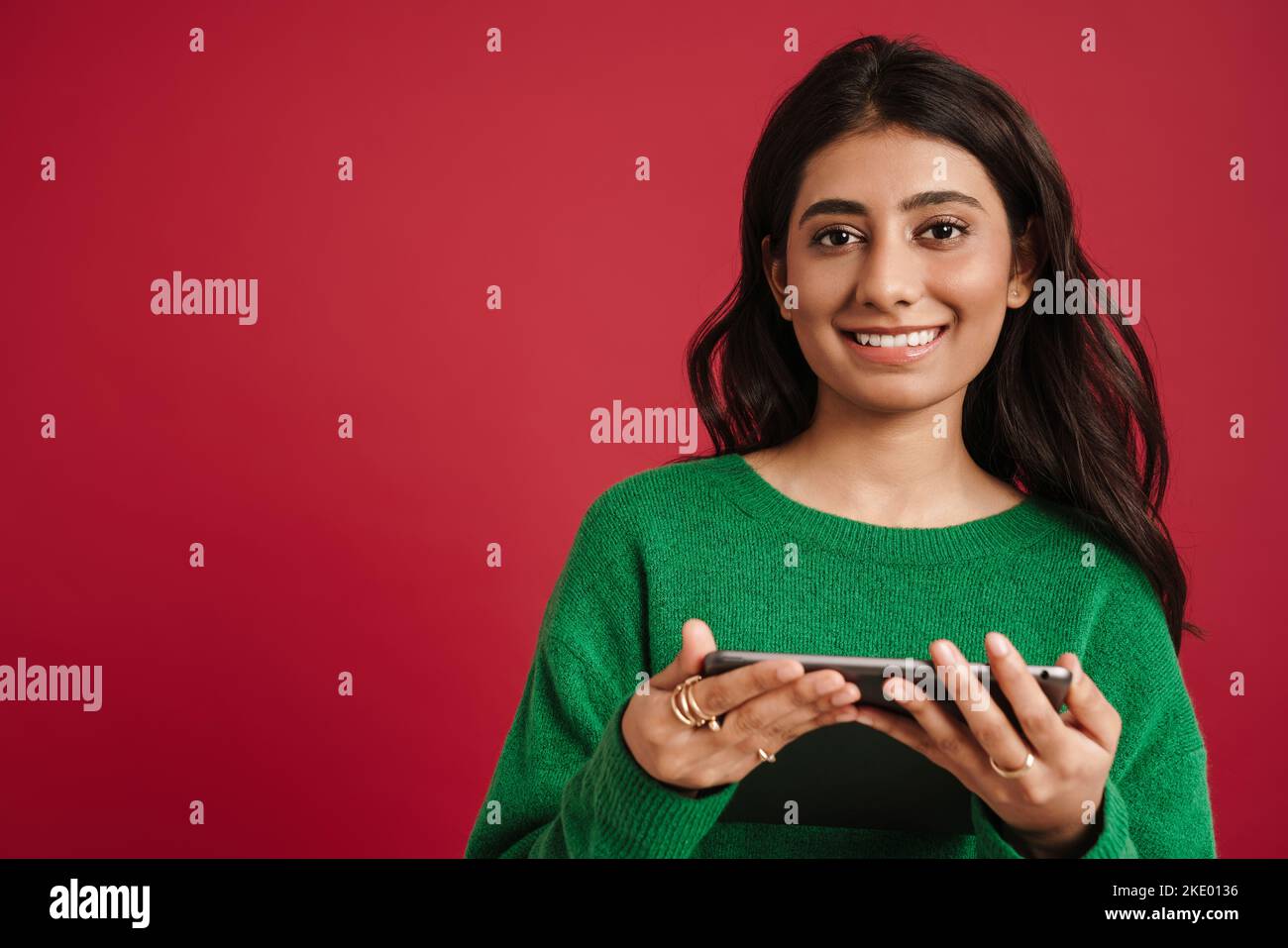 Young indian woman smiling and using tablet computer isolated over red ...