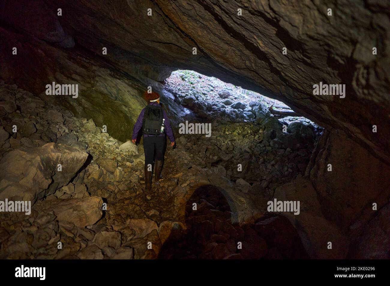 Woman with backpack hiking into a cave underground Stock Photo - Alamy