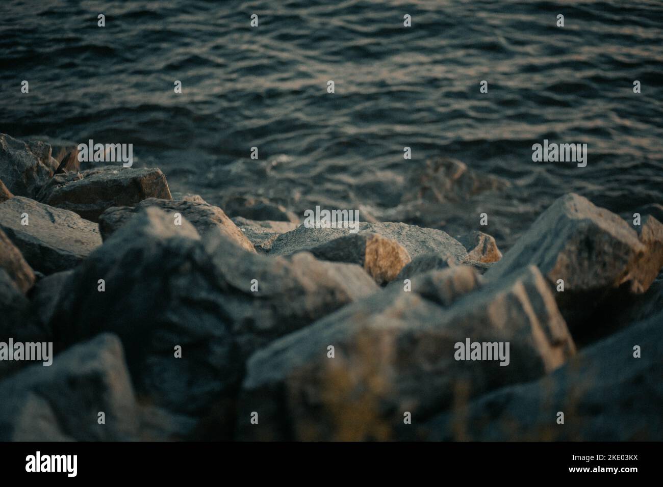 A selective focus of a pile of rocks on the coast, with calm sea in the ...