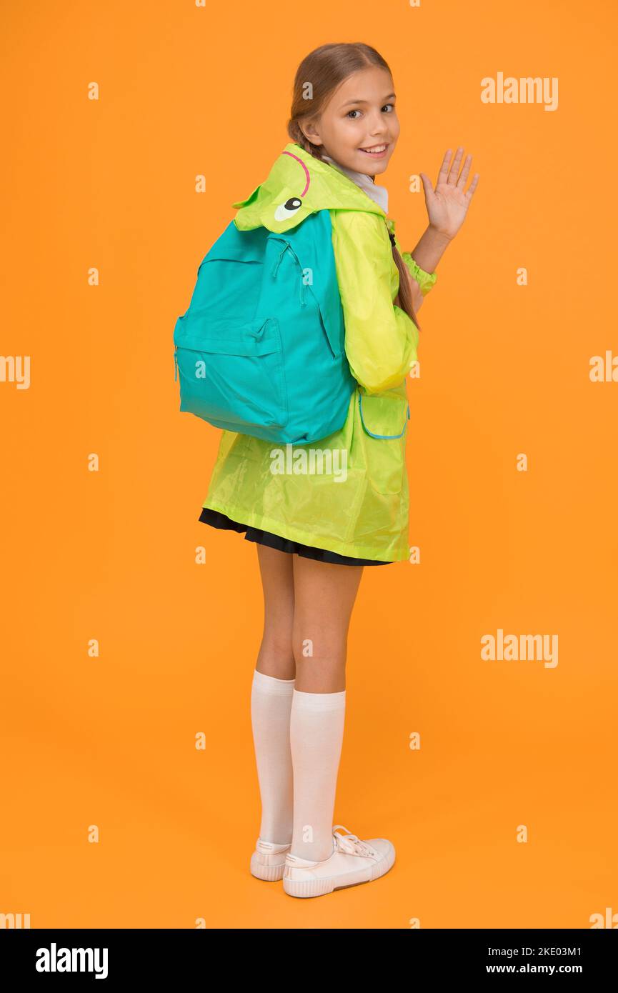 Rain is not hindrance. Schoolgirl raincoat going to school waving hand ...