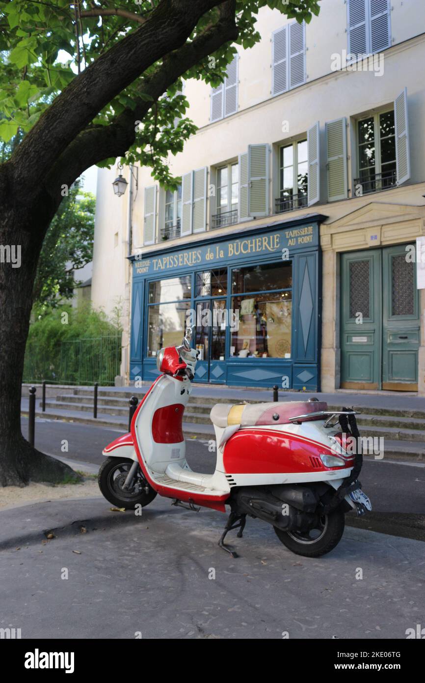 A red and white scooter in Paris on the street under a tree in front of ...