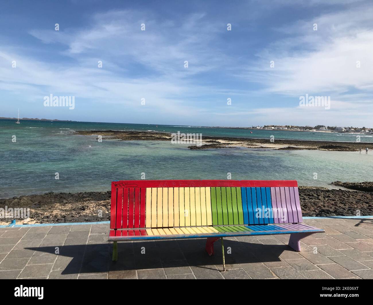 A cute, colorfully painted seat on a paved walkway by the sea under a ...