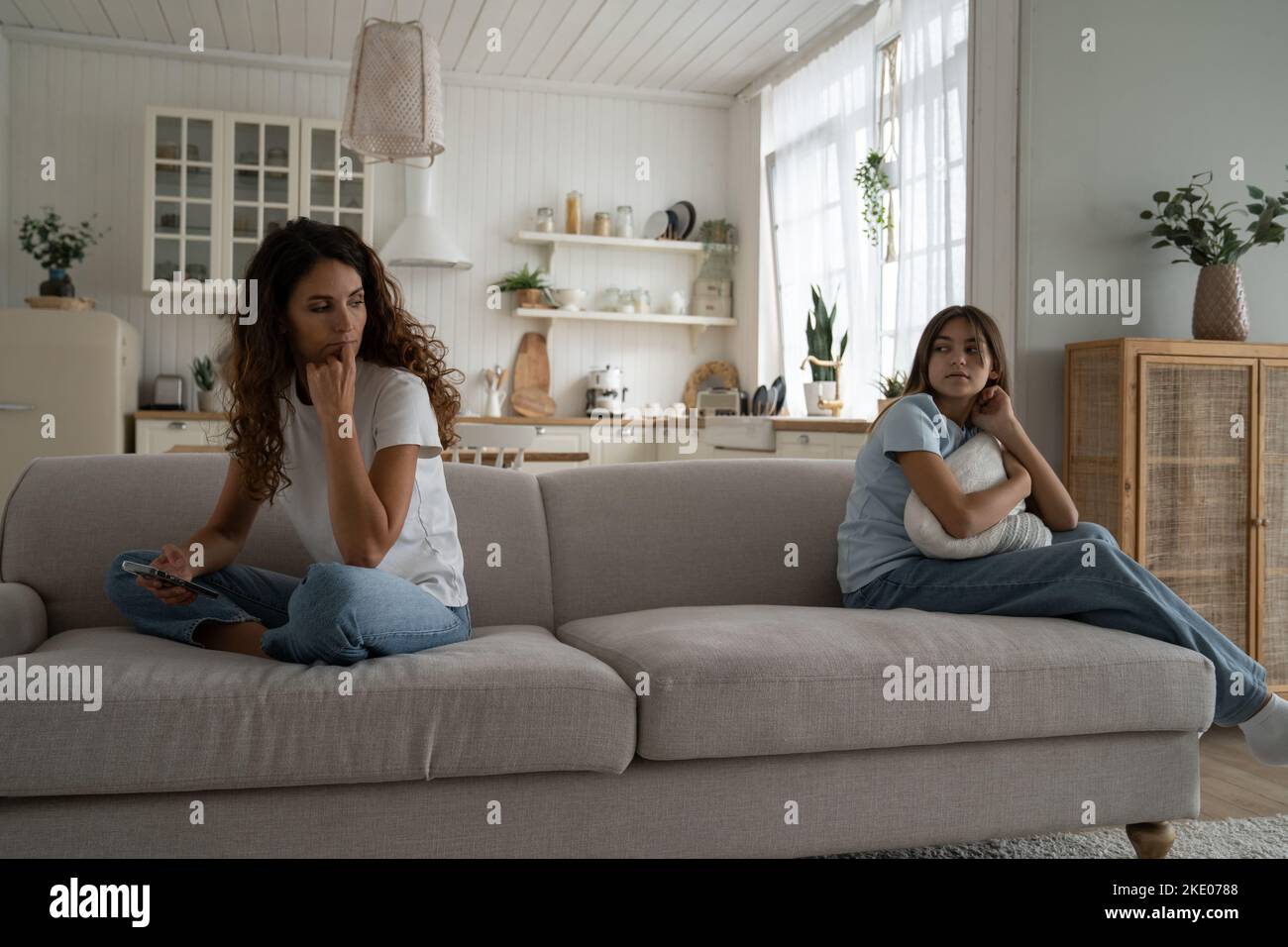 Upset Quarreled Woman And Girl Sit On Opposite Sides Of Sofa In Living