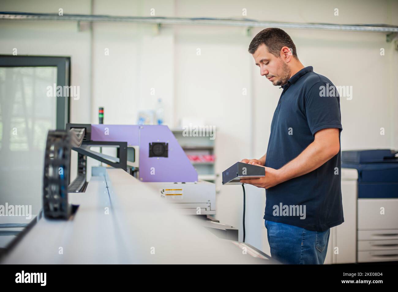 In the printing house, an experienced technician works on a UV printer ...