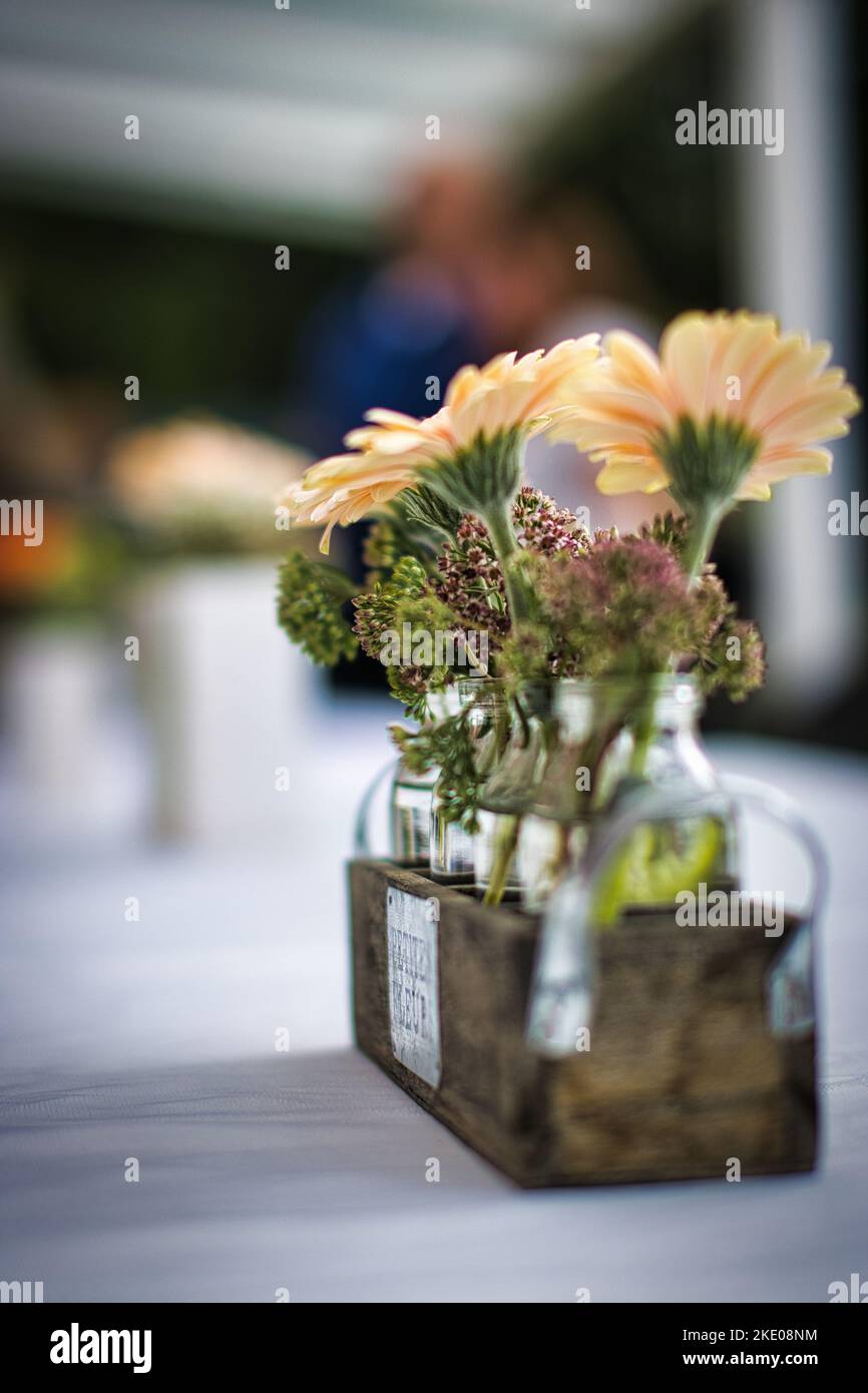 A vertical view of decorative flowers in glass bottles in a wooden box ...