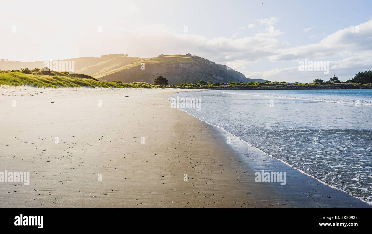 A calm coastline and a blue sea with a scenic view of green hills in ...