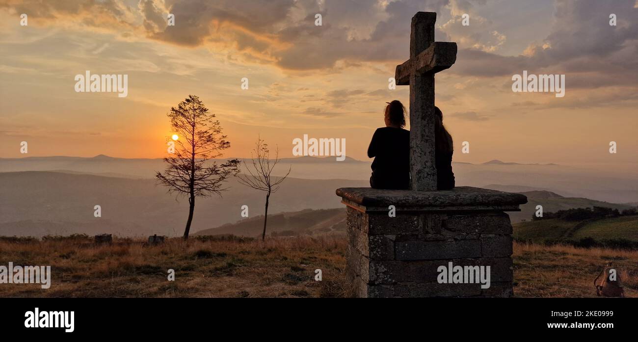A back view of couple sitting on a stone with a cross during orange ...