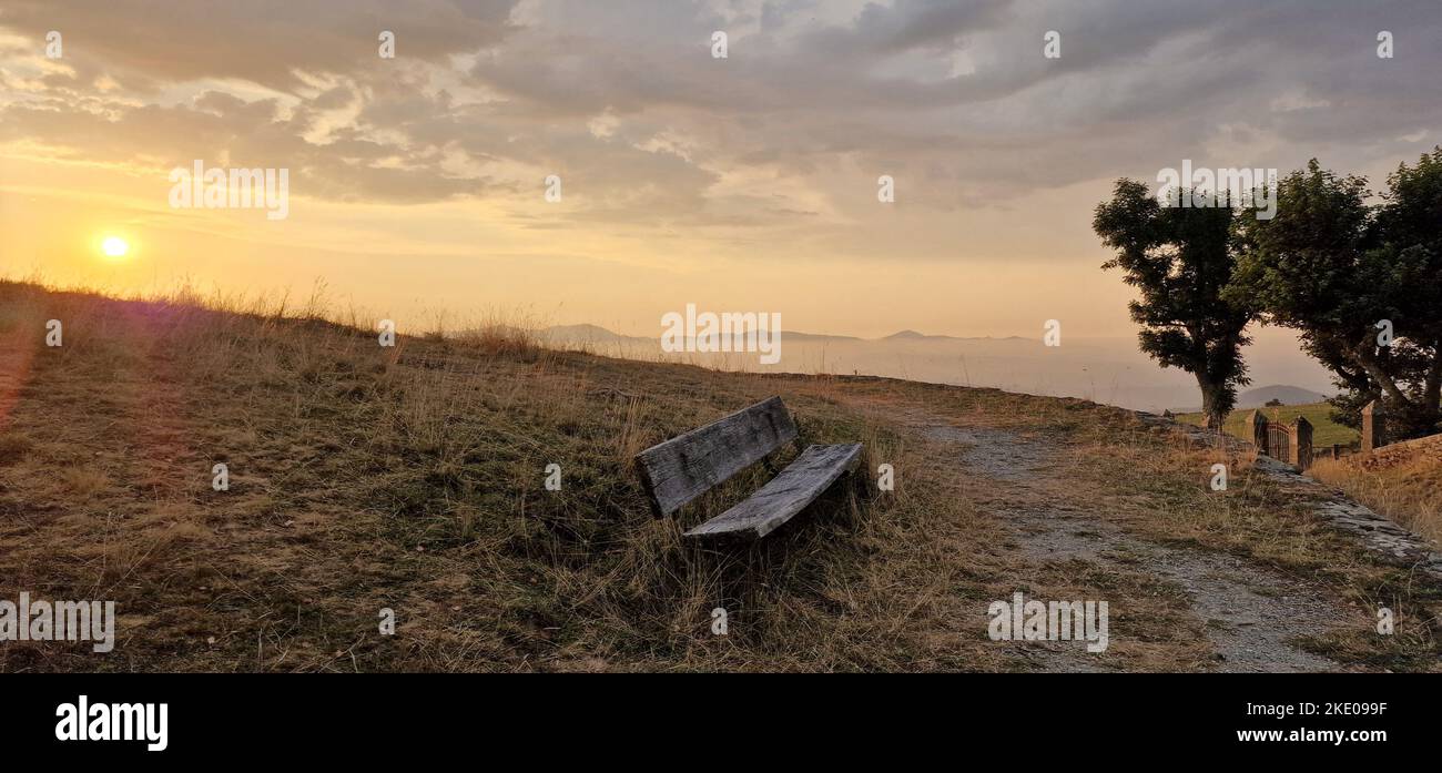 A wooden bench on a hill with dry grass during orange sunset Stock ...