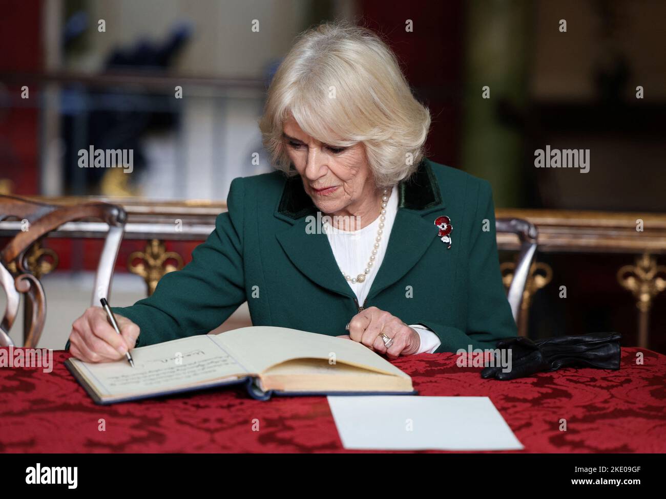 The Queen Consort signs the visitors book as she arrives for a ceremony ...