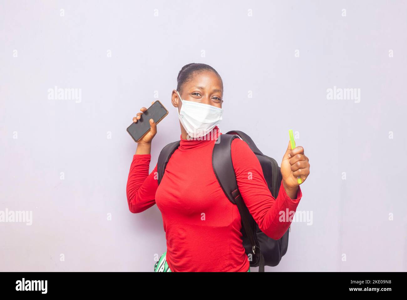 A young African happy female wearing mask and holding mobile phone and ...