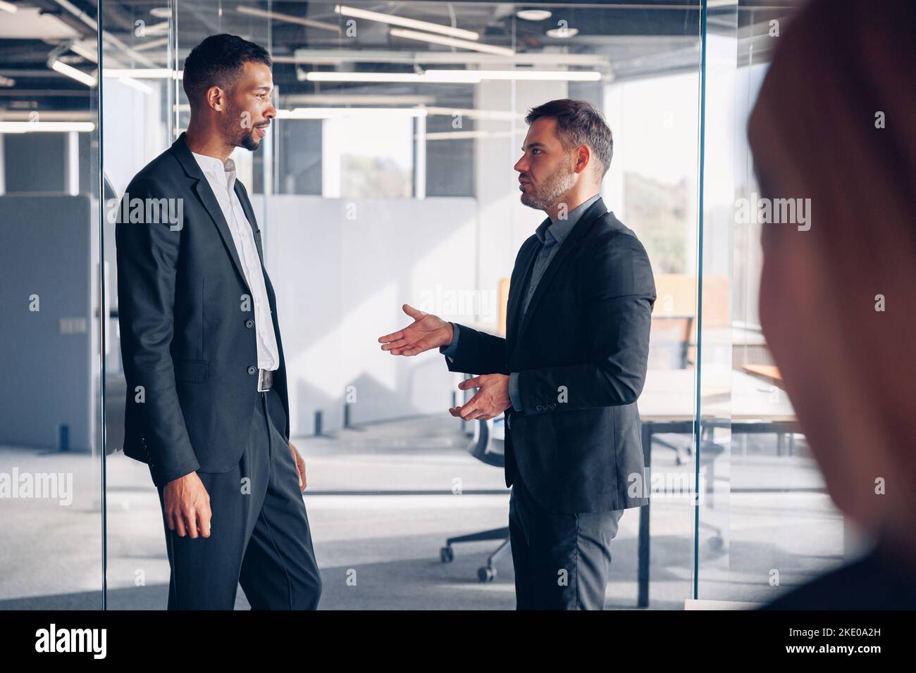 Two business colleagues talking together while standing in meeting room ...