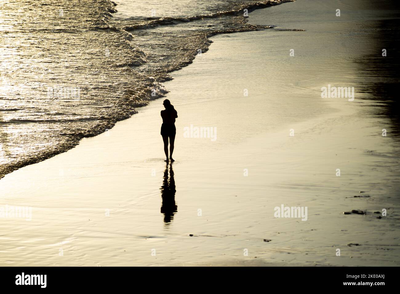 A back view of female silhouette walking on wet Rio Vermelho beach in ...