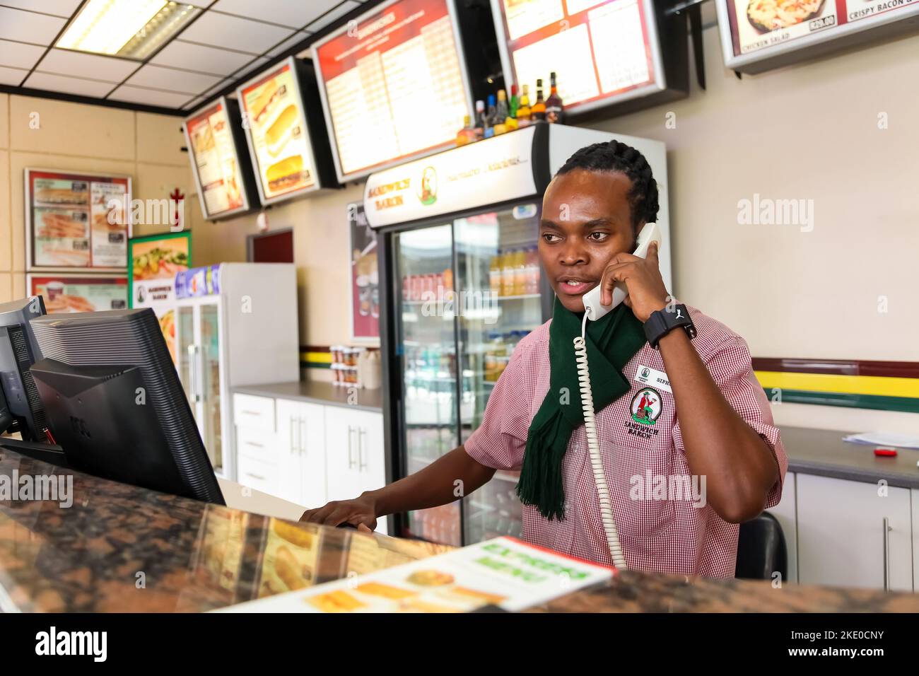 A young black male worker taking a phone order at a fast food ...
