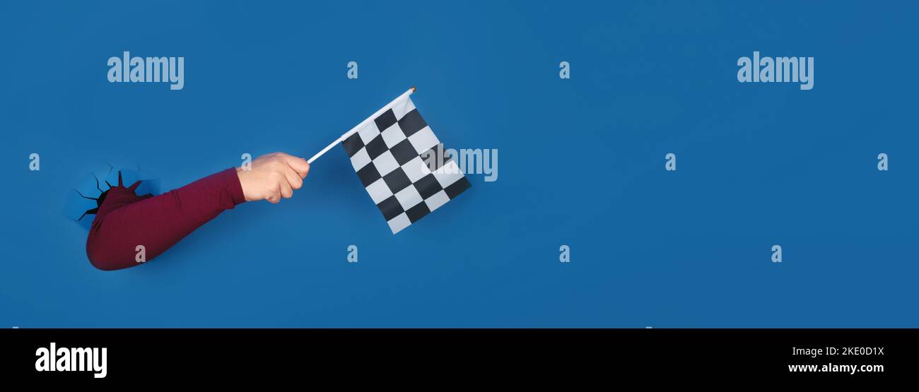 hand holding checkered flag over blue background, panoramic layout ...