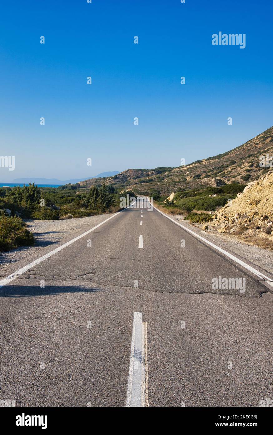 A vertical shot of a highway road with the sea and a blue sky in the ...