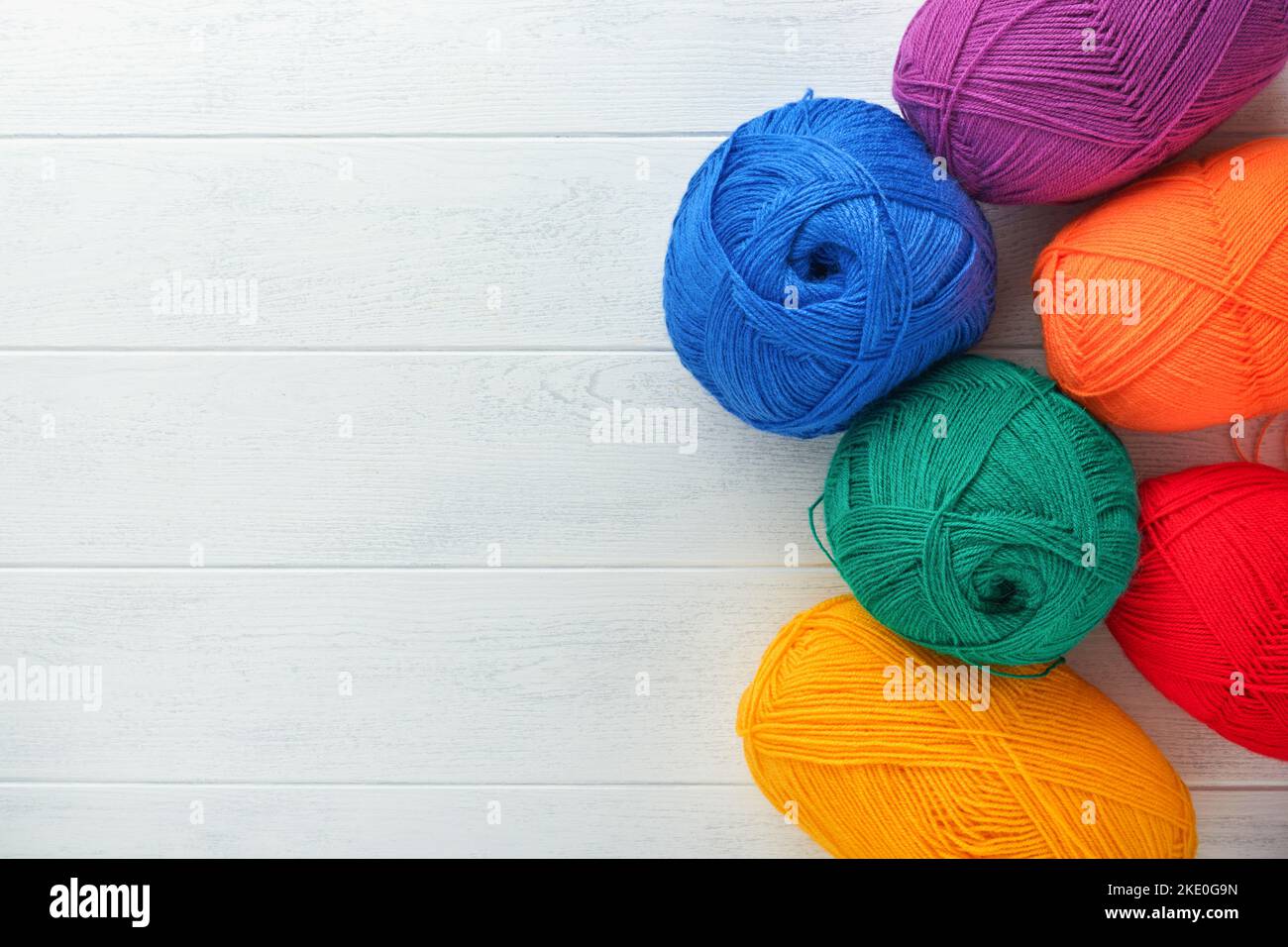 Many multi-colored balls of threads on knitted fabric on white wooden ...