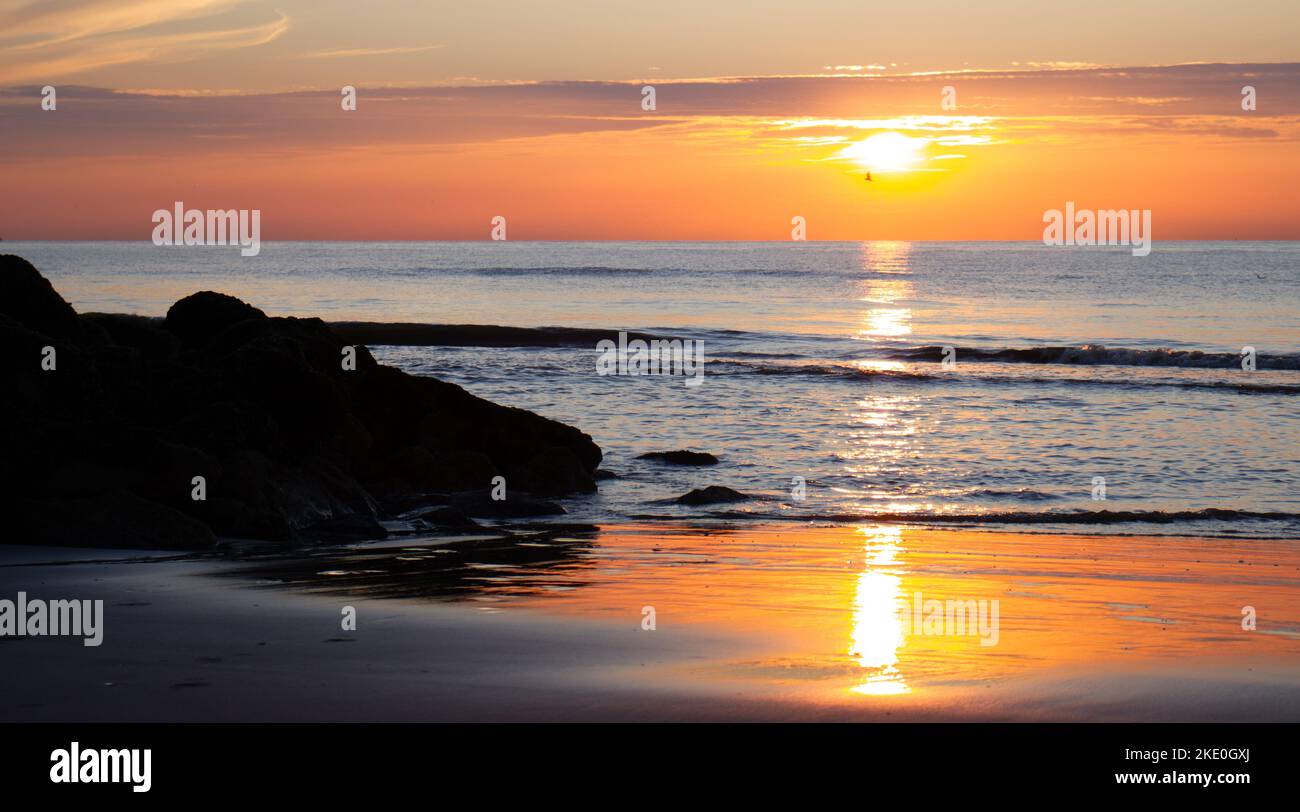 The view of ocean waves touching the sand under the orange sunset sky ...